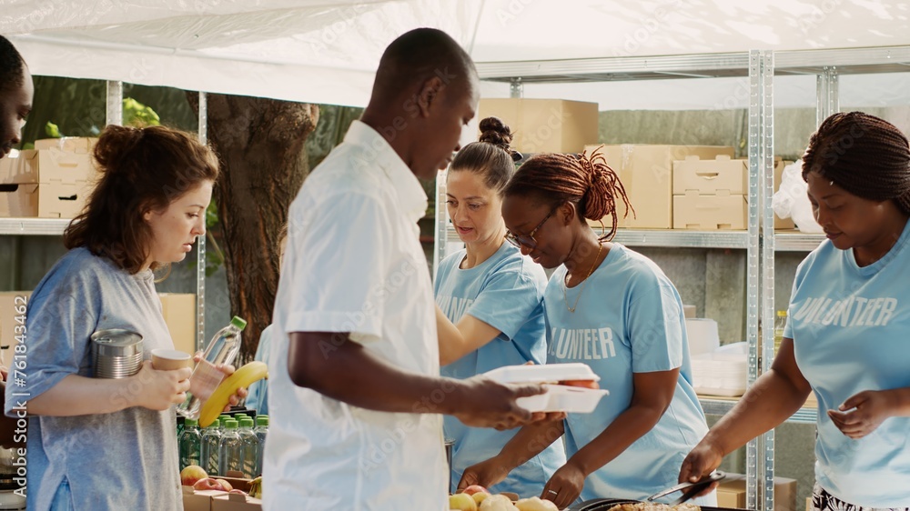 Multiracial volunteer ladies serve meals and non-perishable products to ...