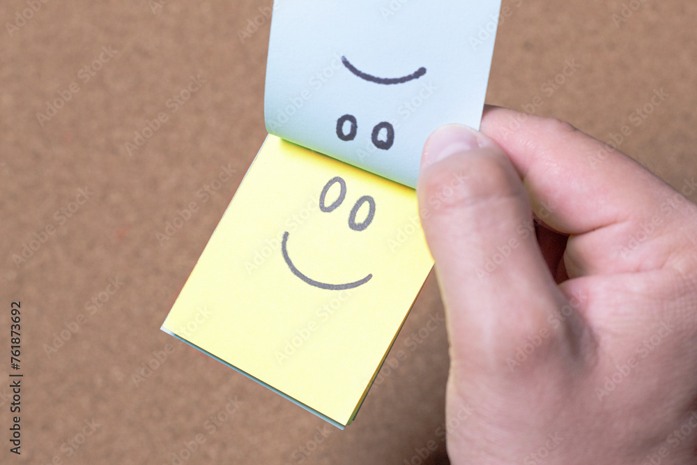 A hand reveals a smiley face on a yellow note that used to be hidden ...