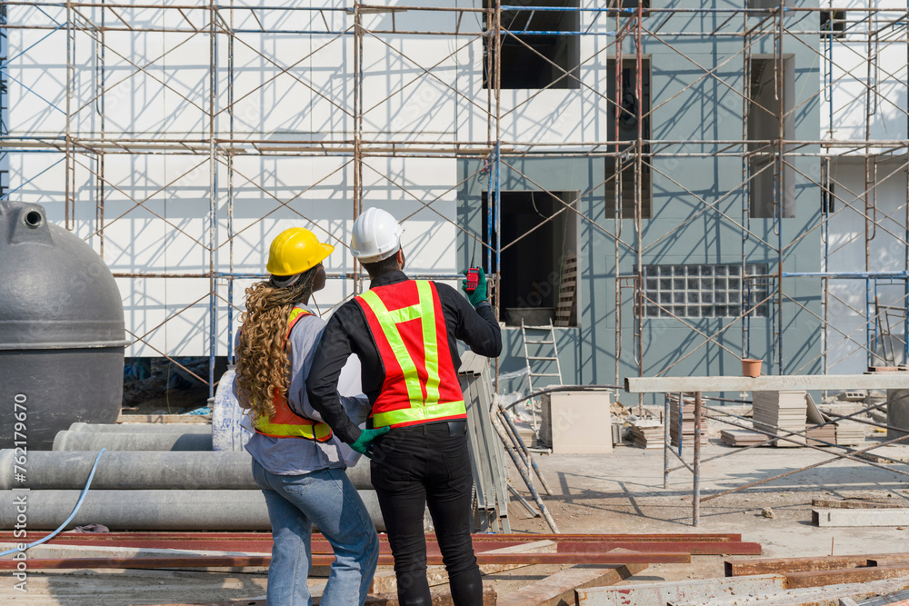 Two construction workers are standing together in front of a large ...