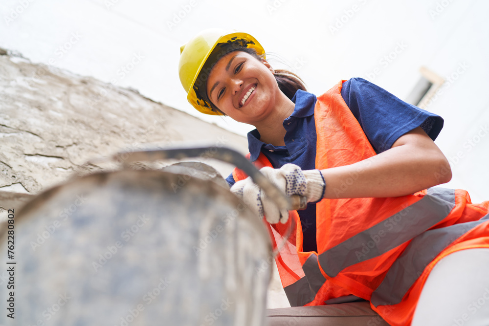 Low angle portrait of happy young female bricklayer with bucket at ...