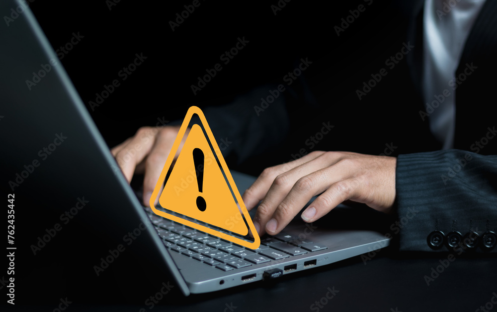 Adult man using computer laptop with triangle caution warning sign for ...