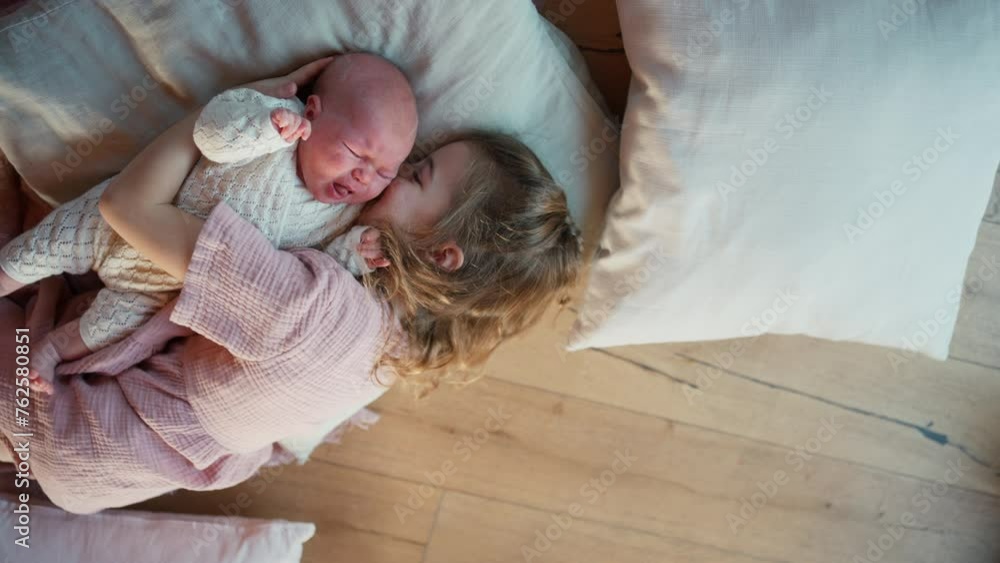 Portrait of big sister cuddling newborn, little baby. Girl lying with ...