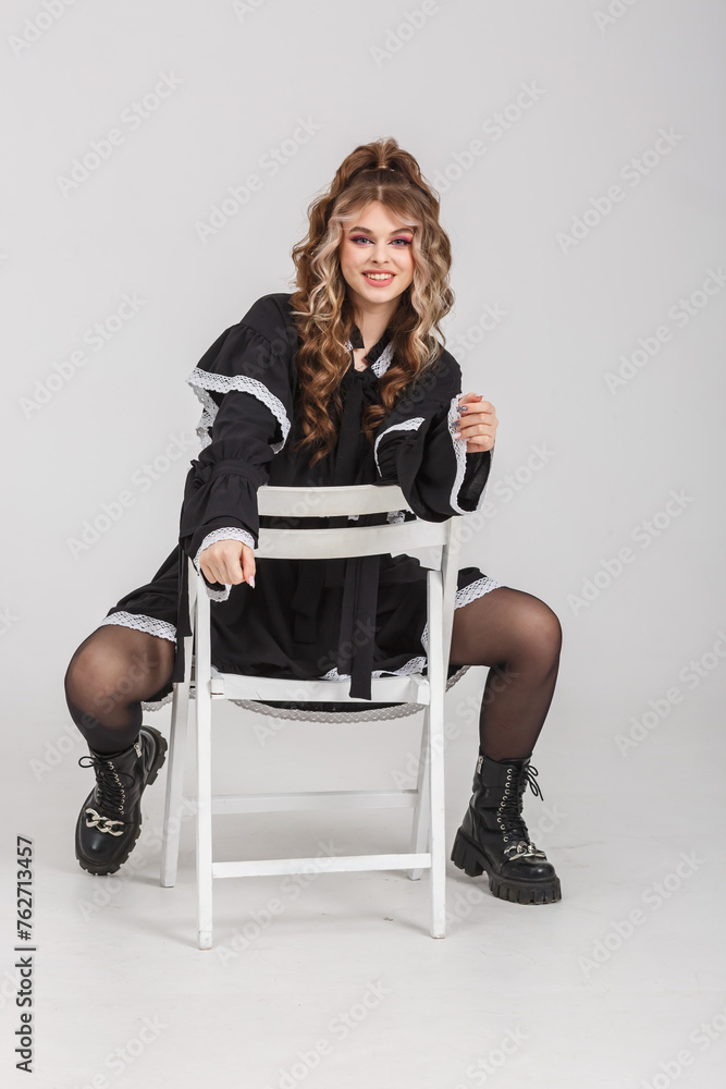 young girl in black school dress poses on chair as doll on white ...
