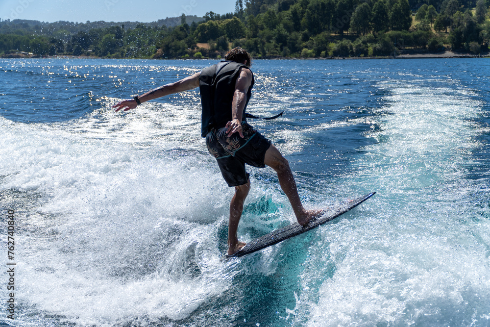 Athletic young man wake surfing on a wave in the lake, spinning mid-air ...