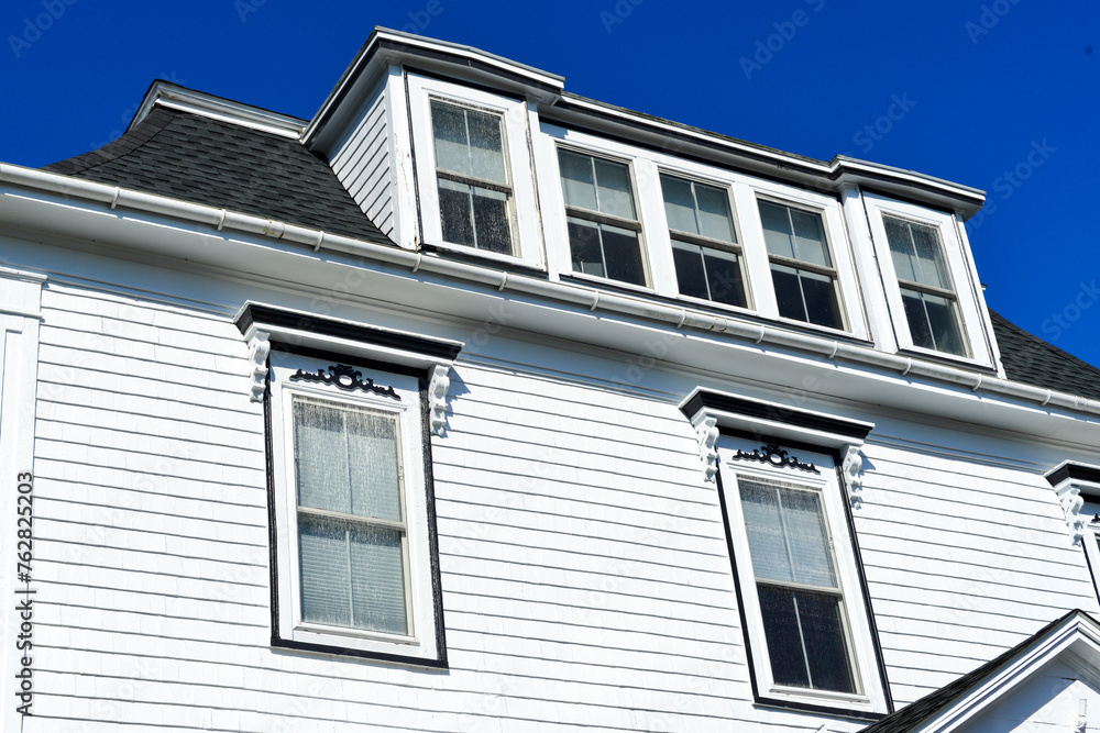 A large vintage Mansard roof on a white wooden house. The attic has a ...