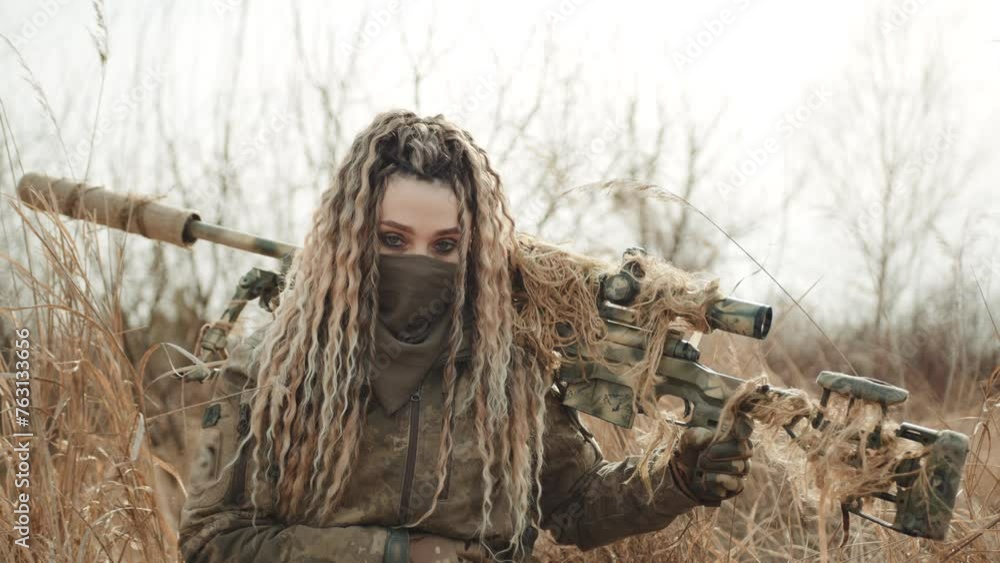 A female soldier equipped with a sniper rifle over her shoulder and a ...