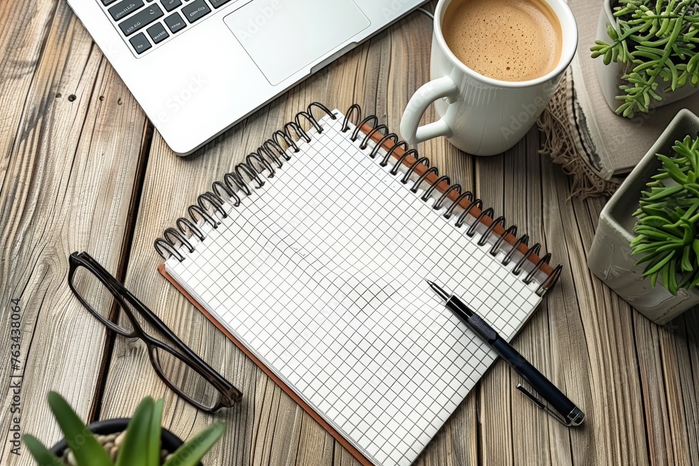 Laptop adjacent to a grid notebook and black pen on wooden slats; a ...