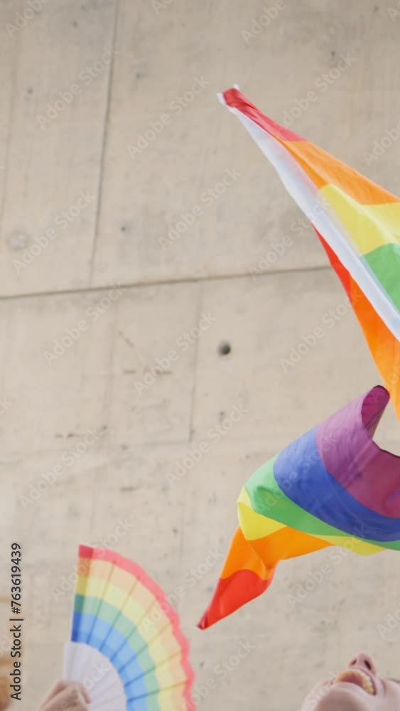 Vertical. LGBT rainbow waving in wind in front of a wall. Hand holding ...