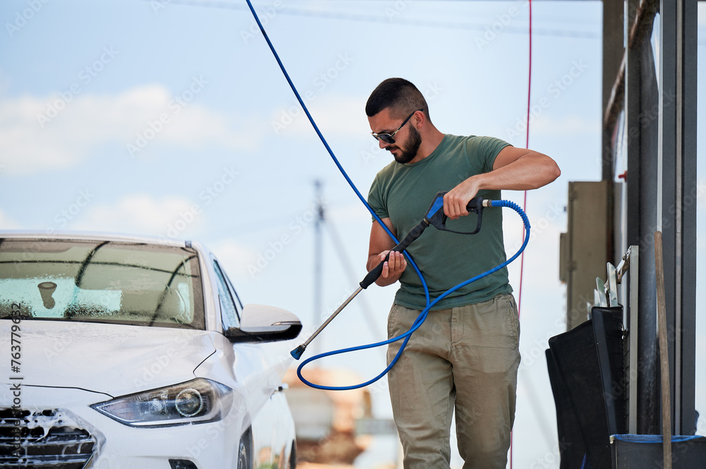 Washing luxury white auto with water gun on an open air car wash ...