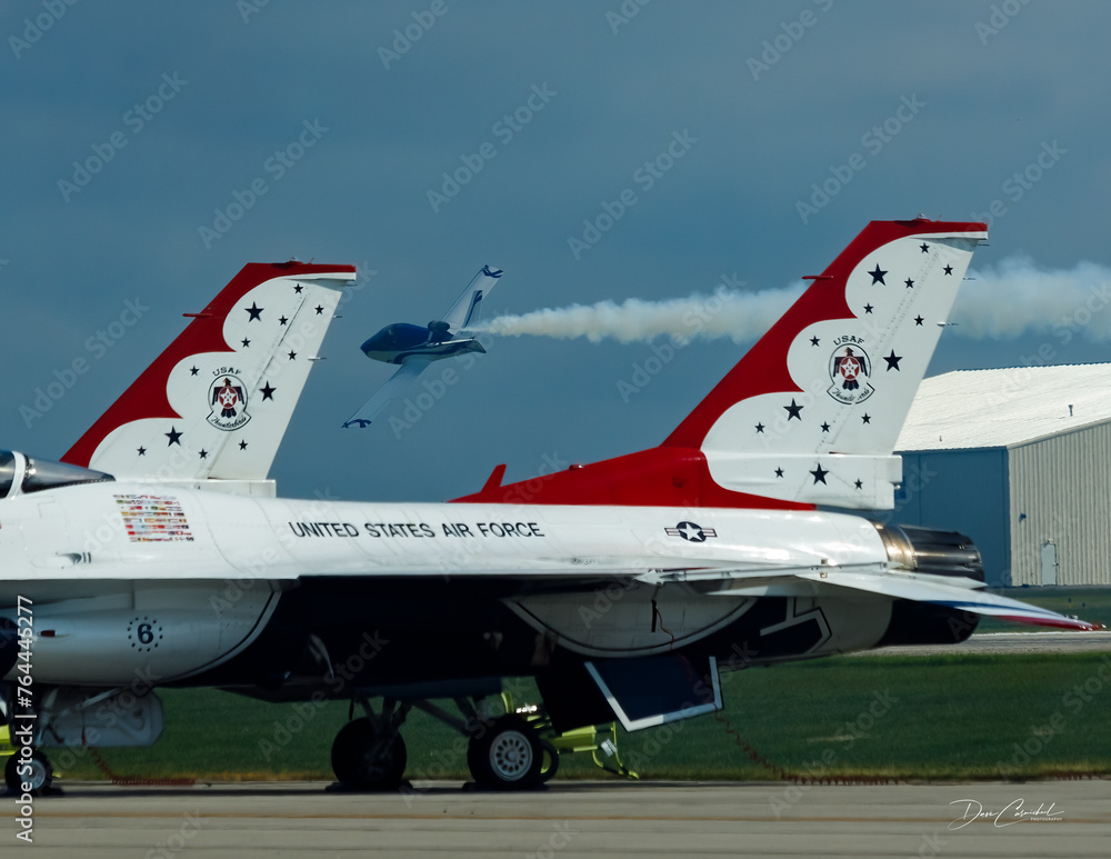 small jet aircraft in flight at an airshow viewed between the tails of ...