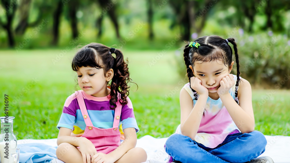 Two little girl expressing boredom face while setting on green grass ...