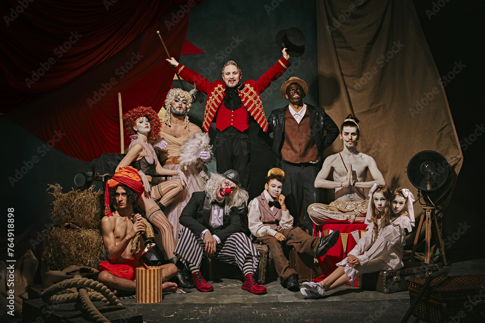 Diverse cast of vintage circus performers poses over dark retro circus ...