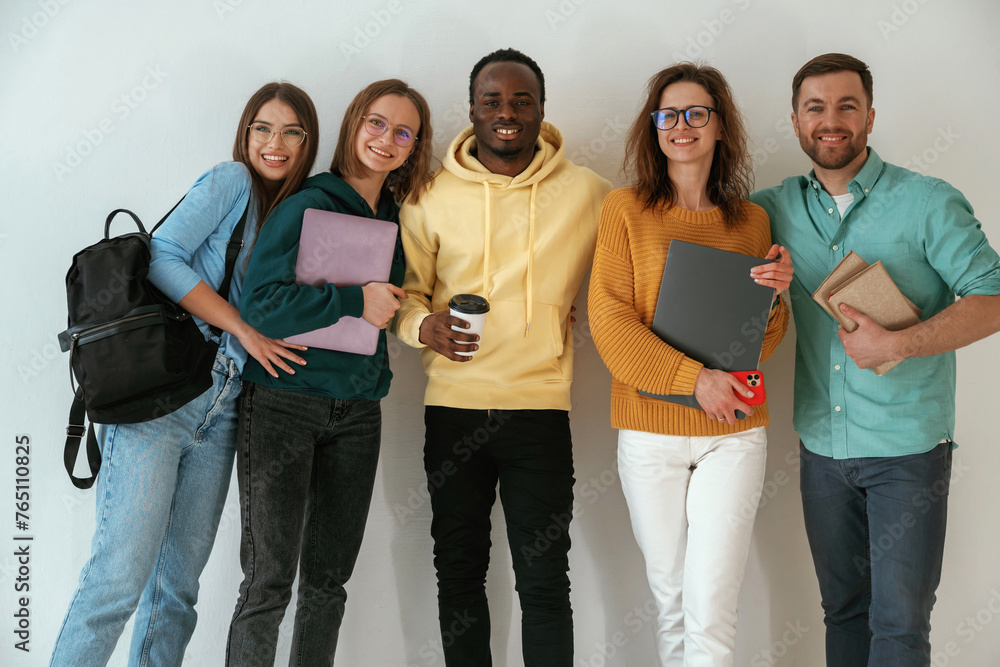 Holding notepads and coffee cup. Group of young people are standing ...