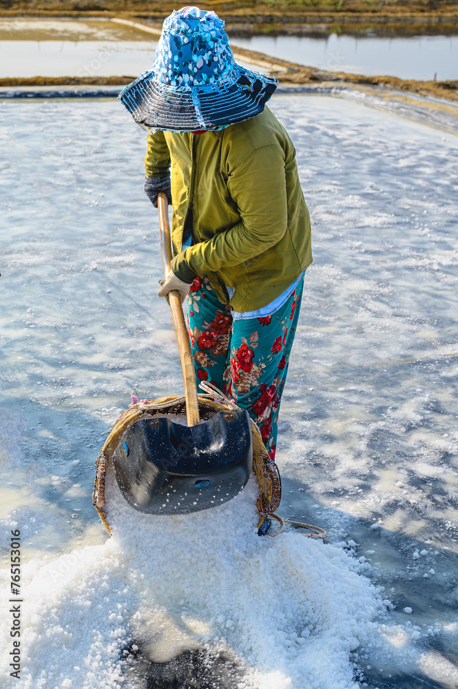 A woman is raking salt into baskets to transport salt to the warehouse ...