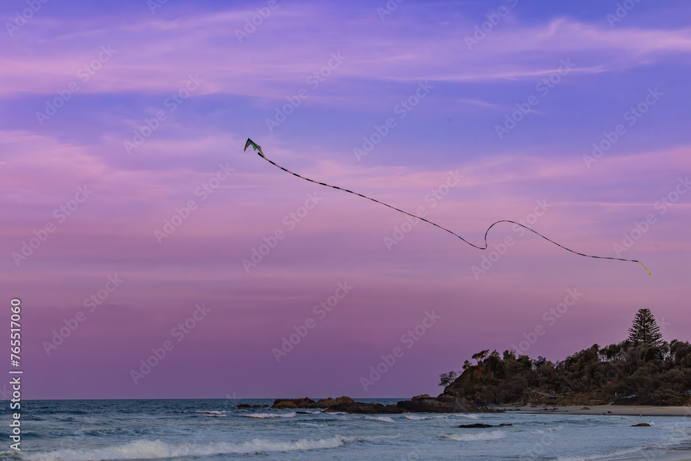 Kite flying over the beach through pink and purple sunset sky with long ...