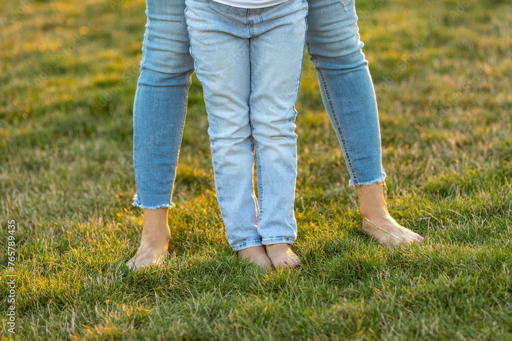 Little daughter and young adult mother walk barefoot on fresh green ...