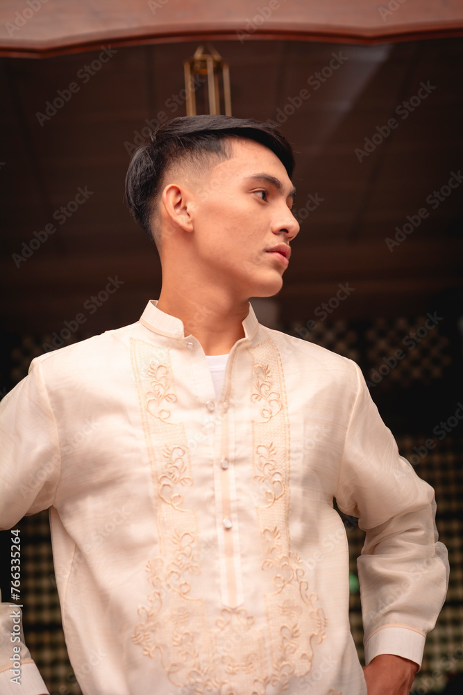 A young FIlipino man wearing a traditional Barong Tagalog shirt, inside ...