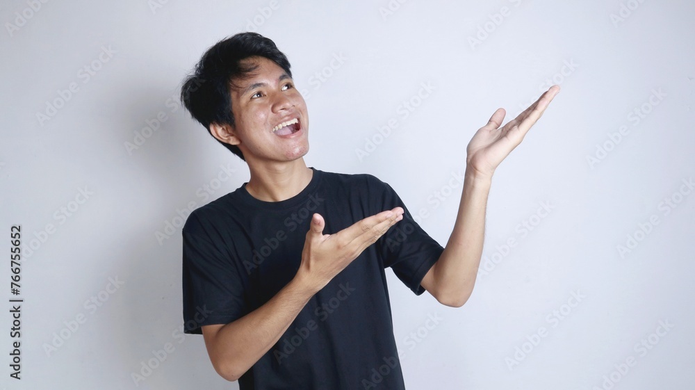 Young Asian man smiling gesturing with open palm pointing to the left ...