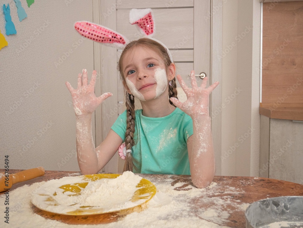 A little girl in rabbit ears at the table shows her hands stained with ...