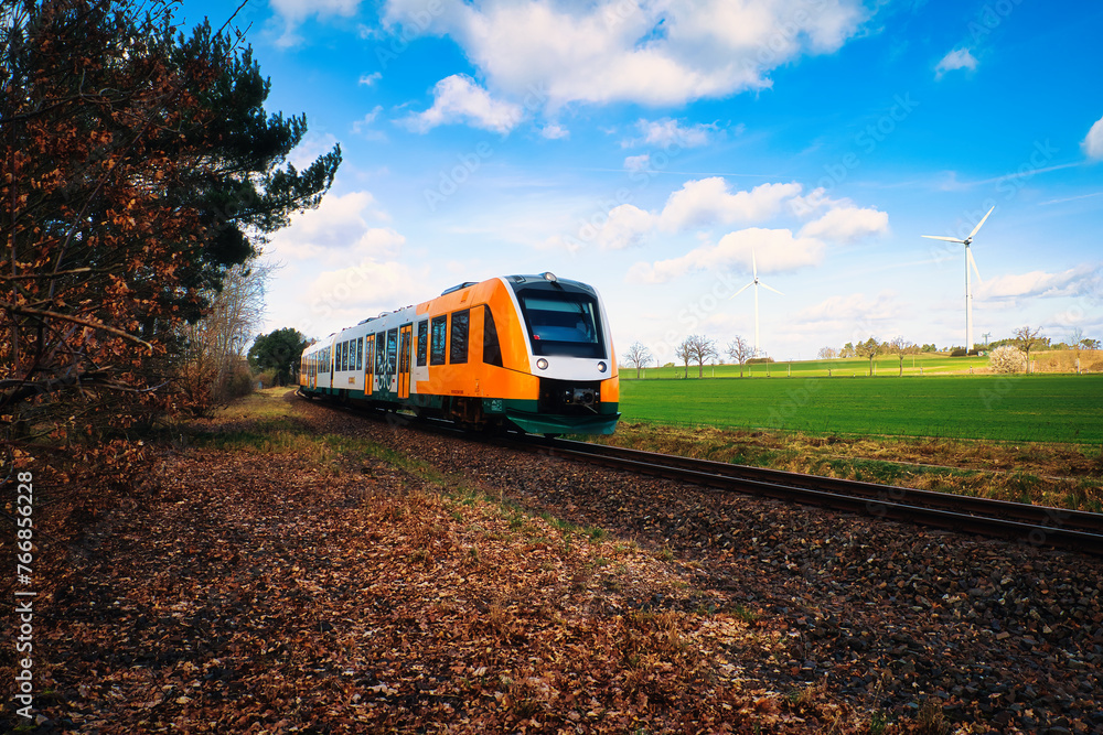 Regionalbahn mit grünem Feld , Wolken und Windkraft im Hintergrund ...
