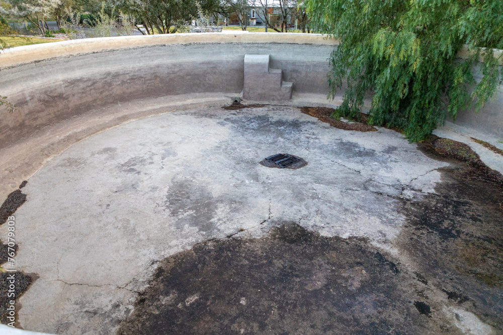 Part of an empty large round concrete pool. At the bottom of the pool ...