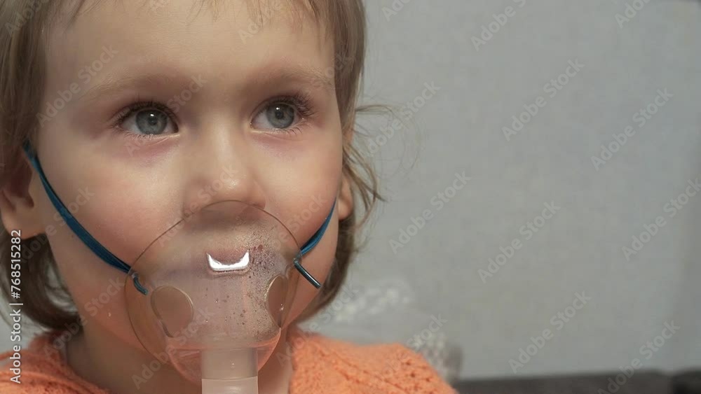 A close-up view of a little girl sitting and holding a nebulizer mask ...