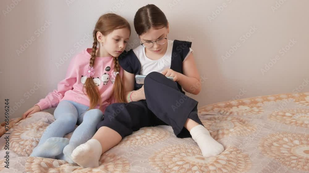 Two little sister girls sitting huddled together using a smartphone. A ...