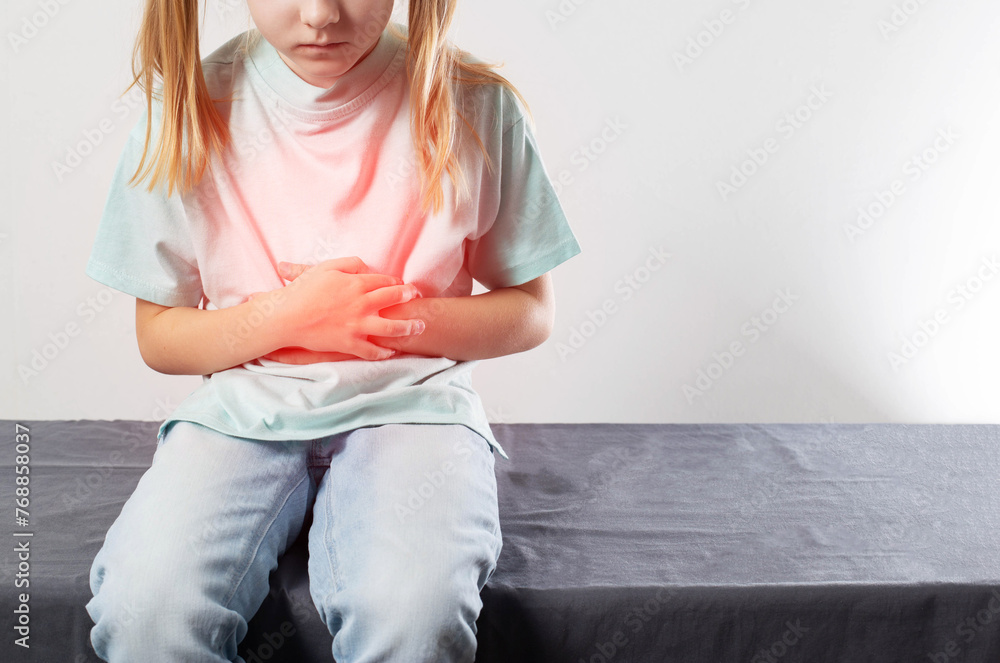 A seven-year-old girl sits and holds her red belly with her hands ...