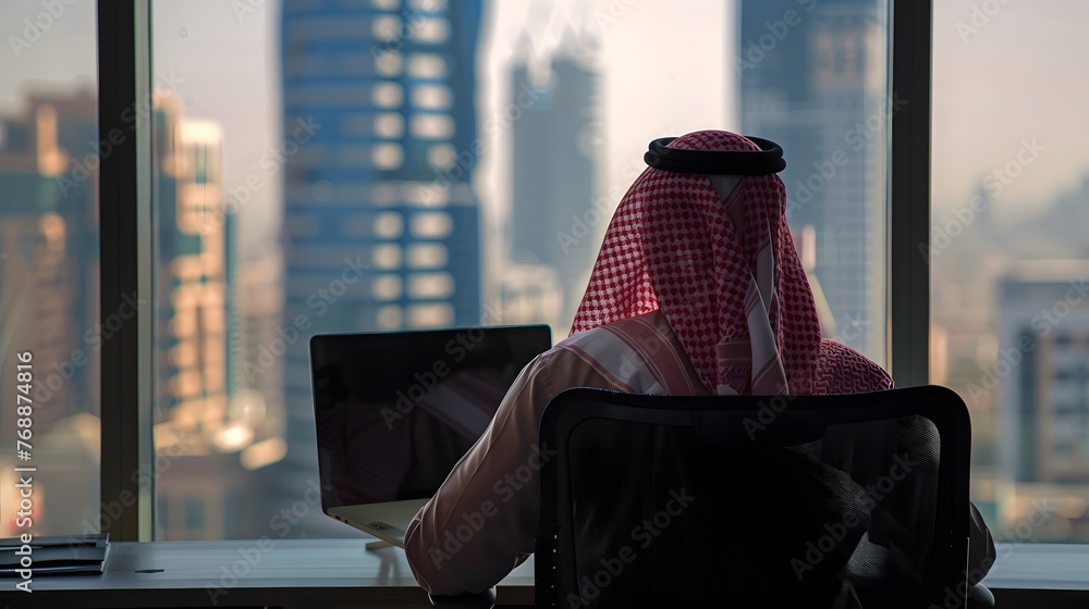 Arab man wearing Saudi bisht, front of laptop, looking at office window ...