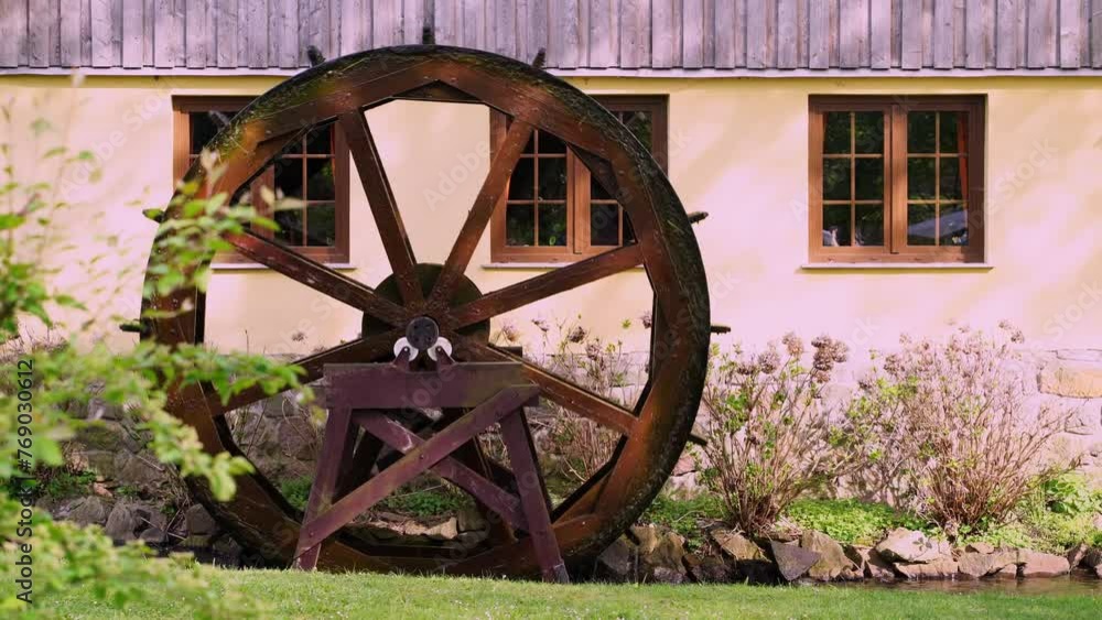 Rotating wooden waterwheel in front of a cream-colored house with ...