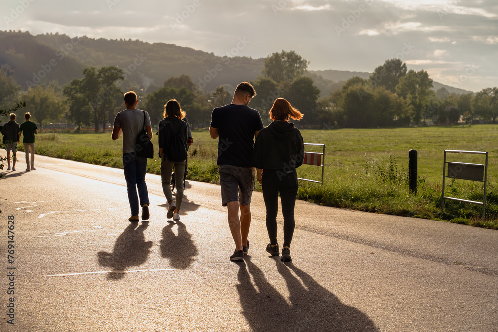 Couples leisurely stroll along a sun-drenched path, their silhouettes ...