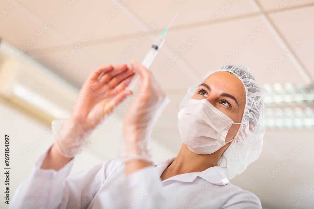 Young nurse in the treatment room prepares a syringe for injection ...