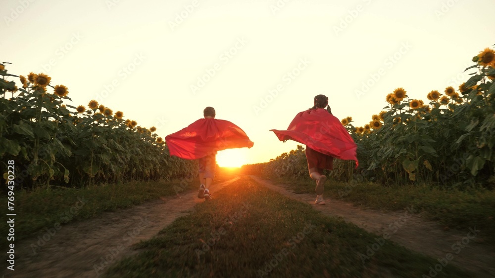Boy and girl superhero in red cloak running flying on road at sunflower ...
