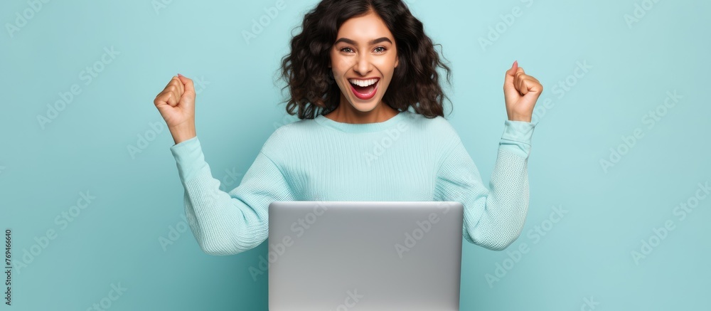 A woman is seated in front of a laptop computer, her arms raised in the ...