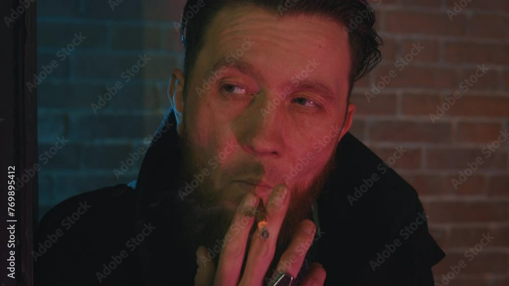 Bearded man is standing around corner of house, smoking, watching ...