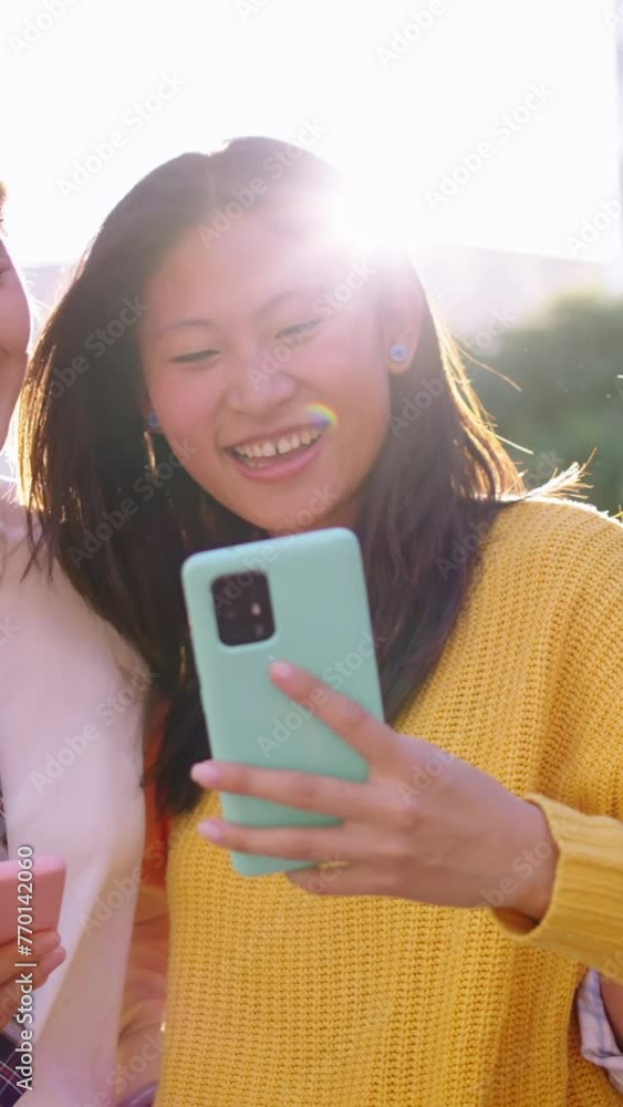Vertical cheerful Asian female friends walk looking laughing cell phone ...