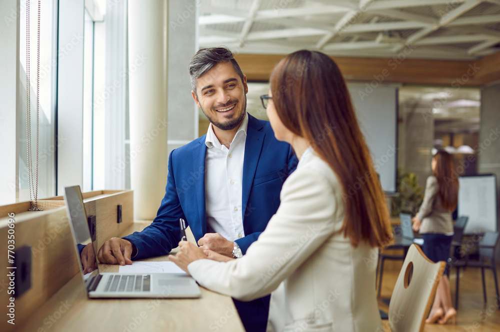 Two young smiling company employees man and woman at the same desk with ...