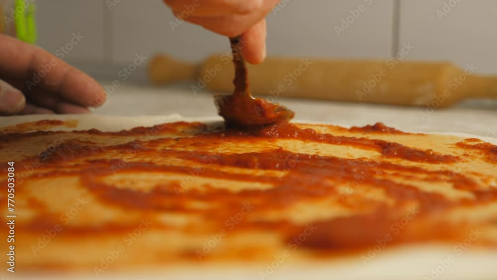Male arm of cook applying ketchup on pizza dough using a spoon at ...