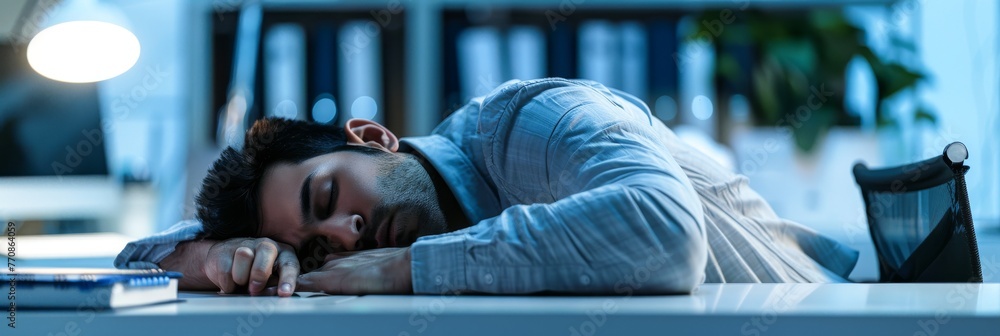 A worker slumped over his desk caught between sleep and work ...