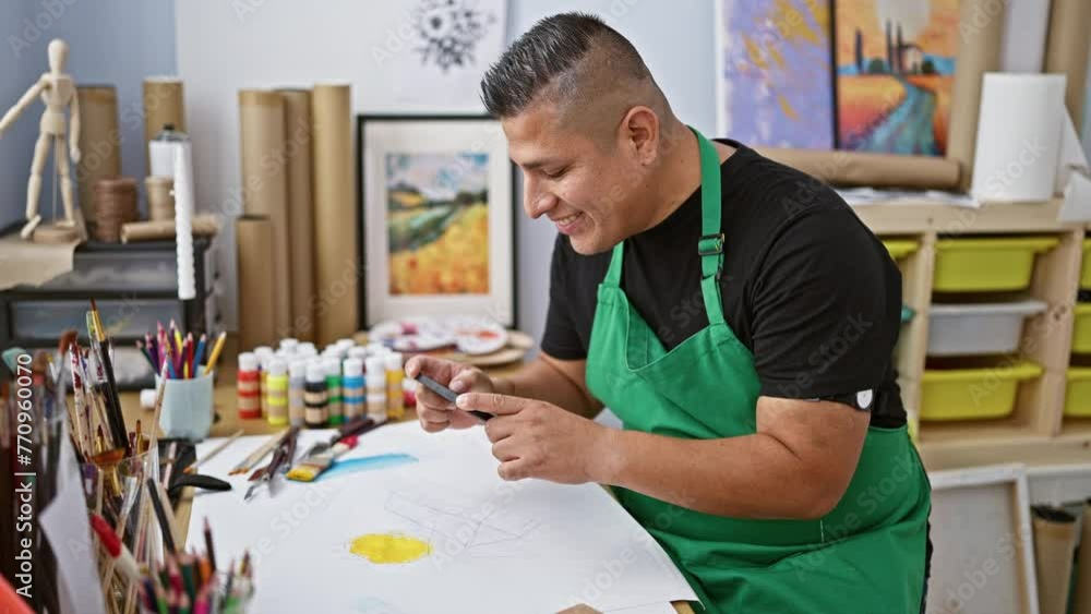 Young, confident latin artist guy making smartphone photos of his art ...