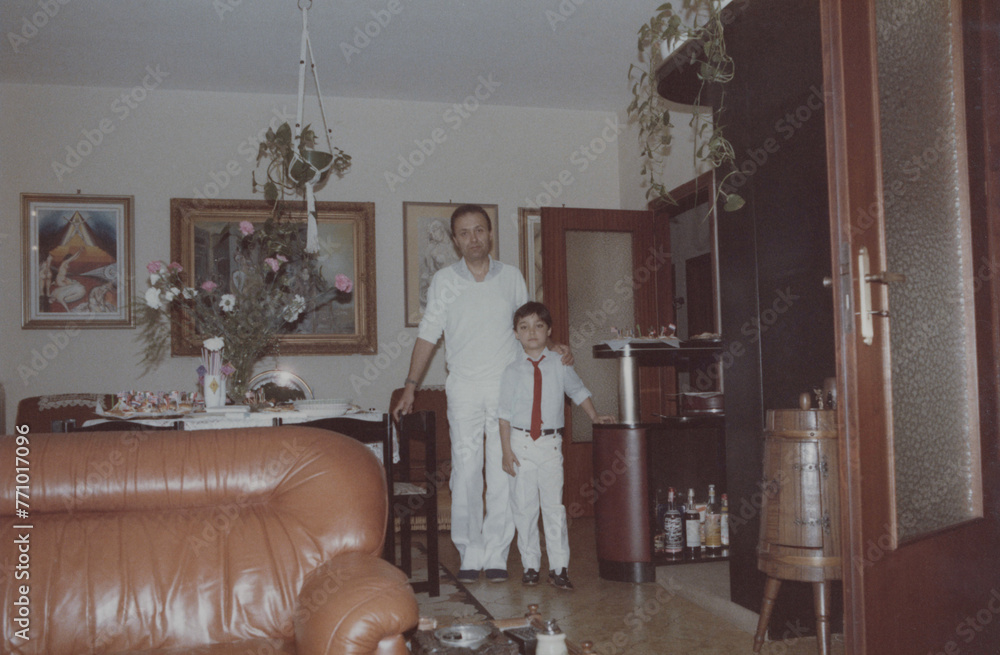 1986. Father and son pose for a photo in the living room of their home ...