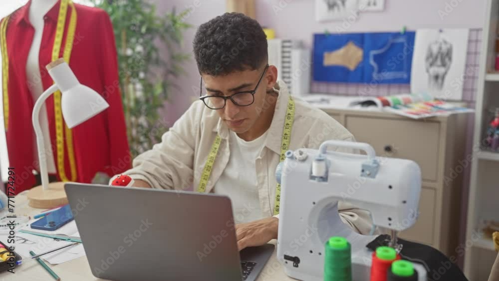A young man tailors clothing in a well-equipped atelier with a sewing ...