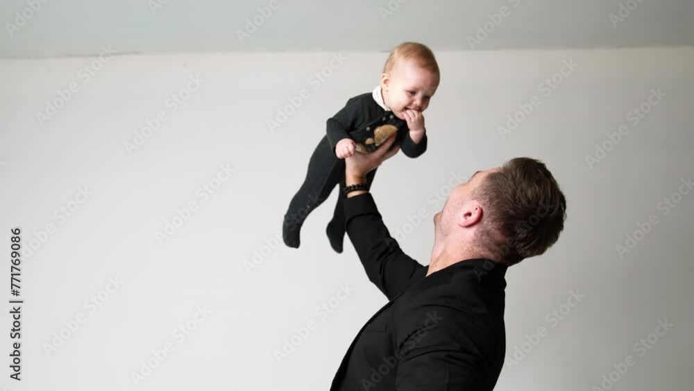 Strong Caucasian man in black jacket holding a baby up with one hand ...