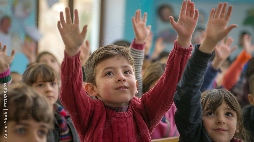 A crowd of happy children in a classroom are raising their hands with ...