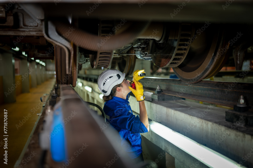 A mechanic in a blue uniform and white helmet intently examines the ...