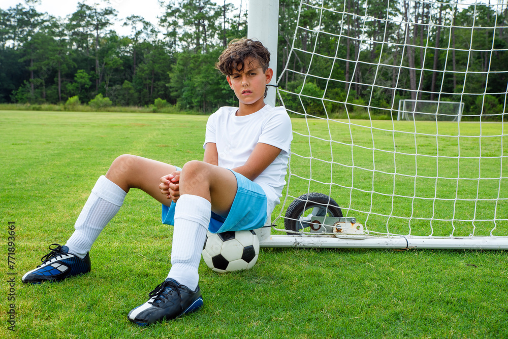 Portrait of a tired youth soccer player sitting on a soccer ball in the ...
