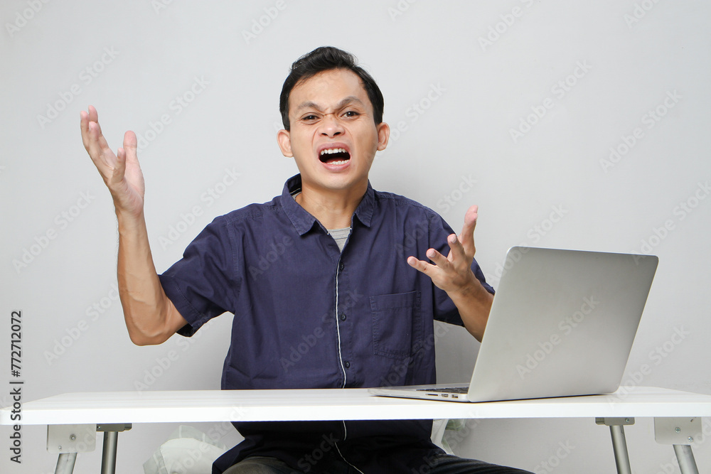 Angry mad asian man in workplace while sitting in front of laptop ...