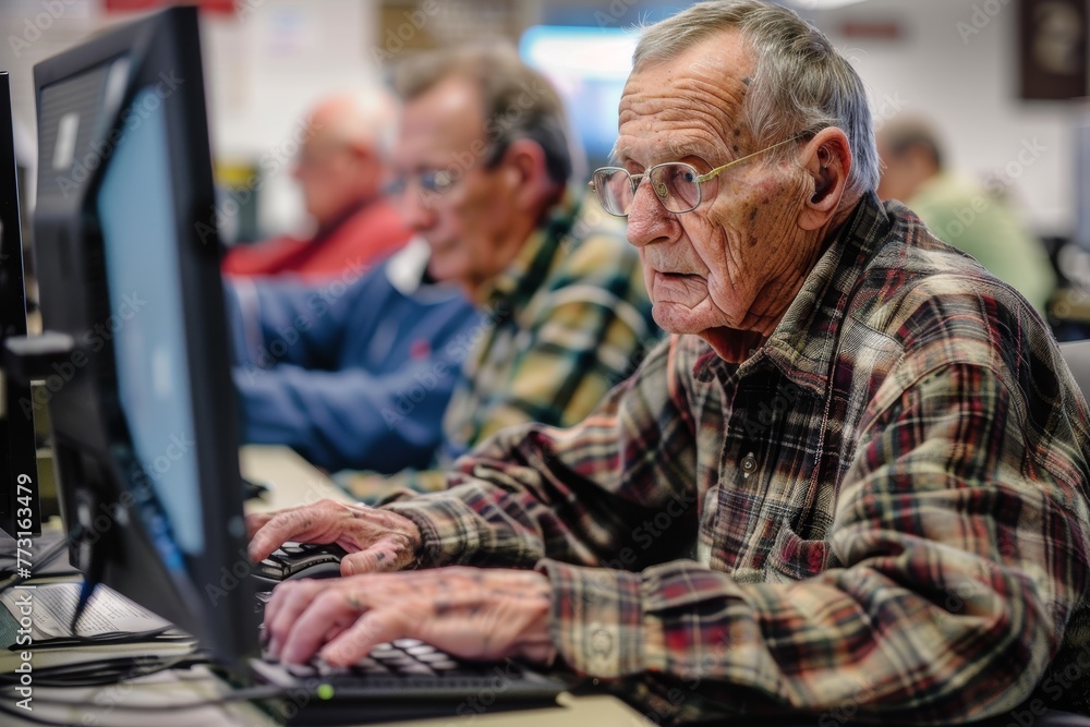 An old man uses a computer atop his desk; another man sits before his ...