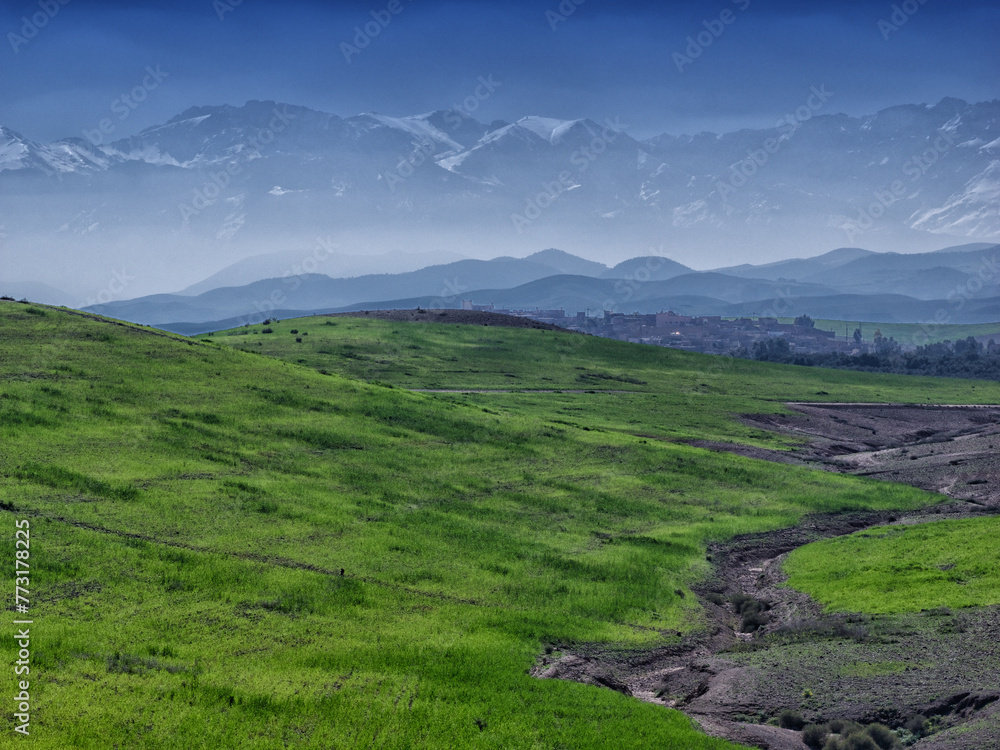 Prairie verte et un oued asséché avec à l'horizon les montagnes de l ...