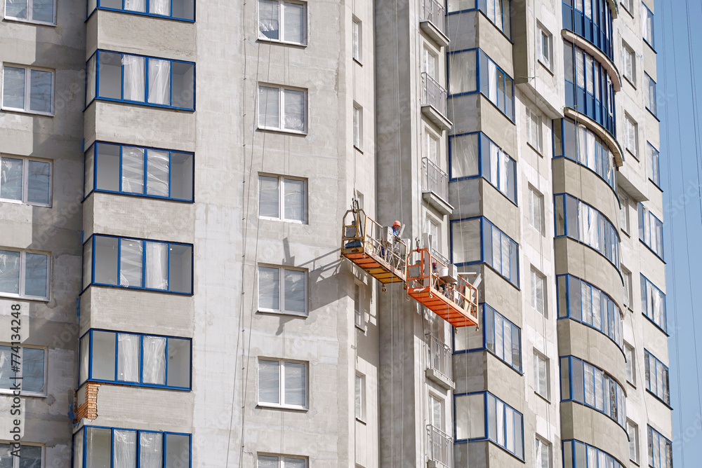 Worker in suspended platform cradle plastering facade wall. Men at work ...